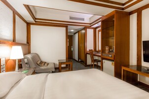 Quarto de hotel com cama, escrivaninha, cadeira, televisão e minibar.