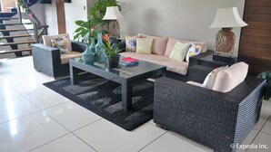Uma sala de estar moderna com uma mesa de centro de vidro, sofás de vime e duas luminárias.