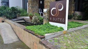 Placa de hotel com 8 suítes, cercado por vegetação e um pequeno espelho d'água.