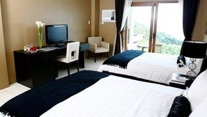 Quarto de hotel com duas camas, uma mesa com computador, uma cadeira, televisão e janela com cortinas.