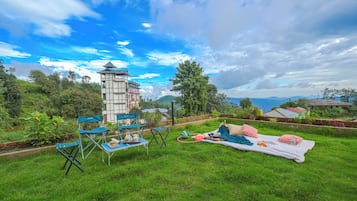 Uma área externa com gramado e um espaço para piquenique, incluindo uma manta, almofadas e uma mesa com bule.