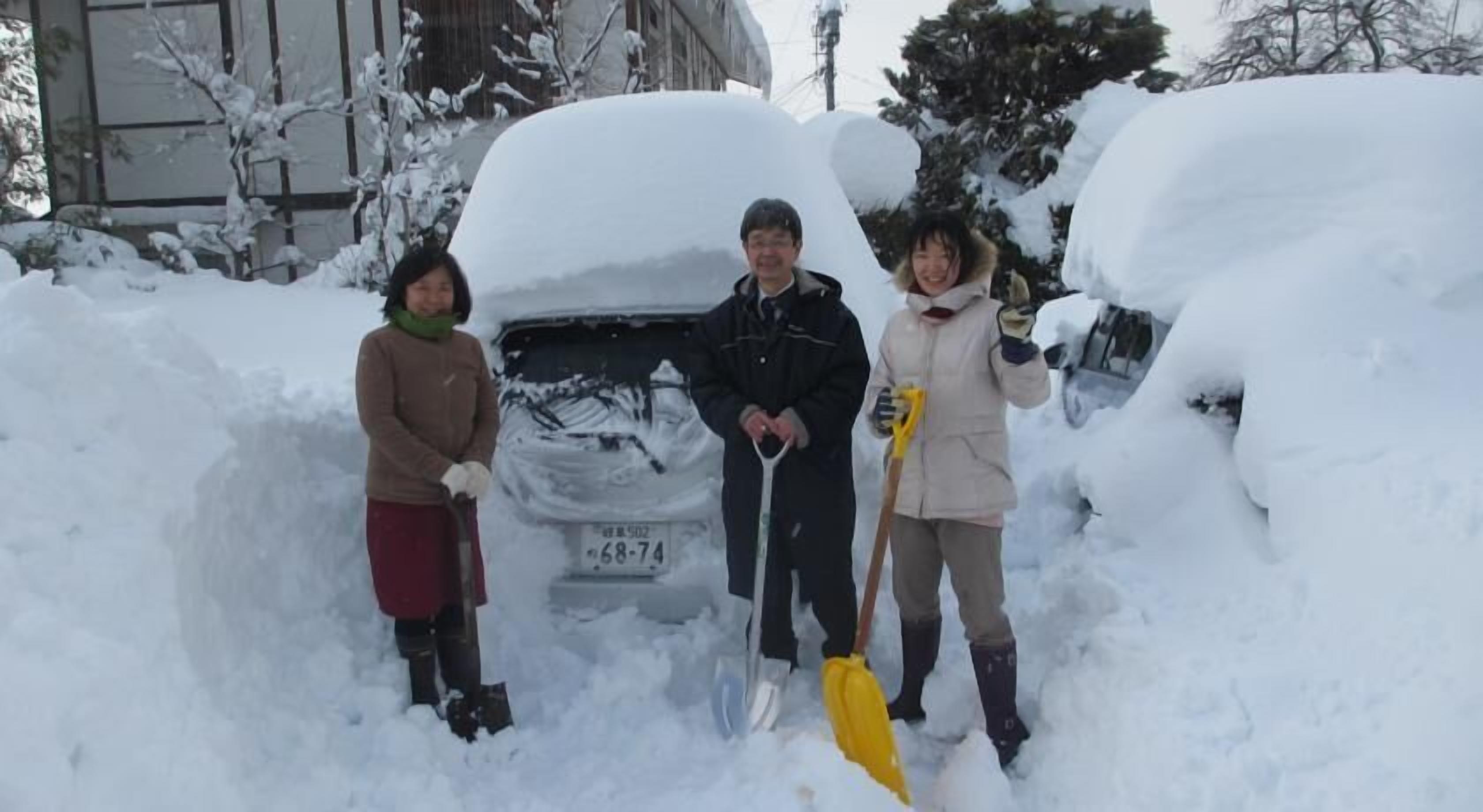 Três pessoas removendo neve da entrada de uma casa.