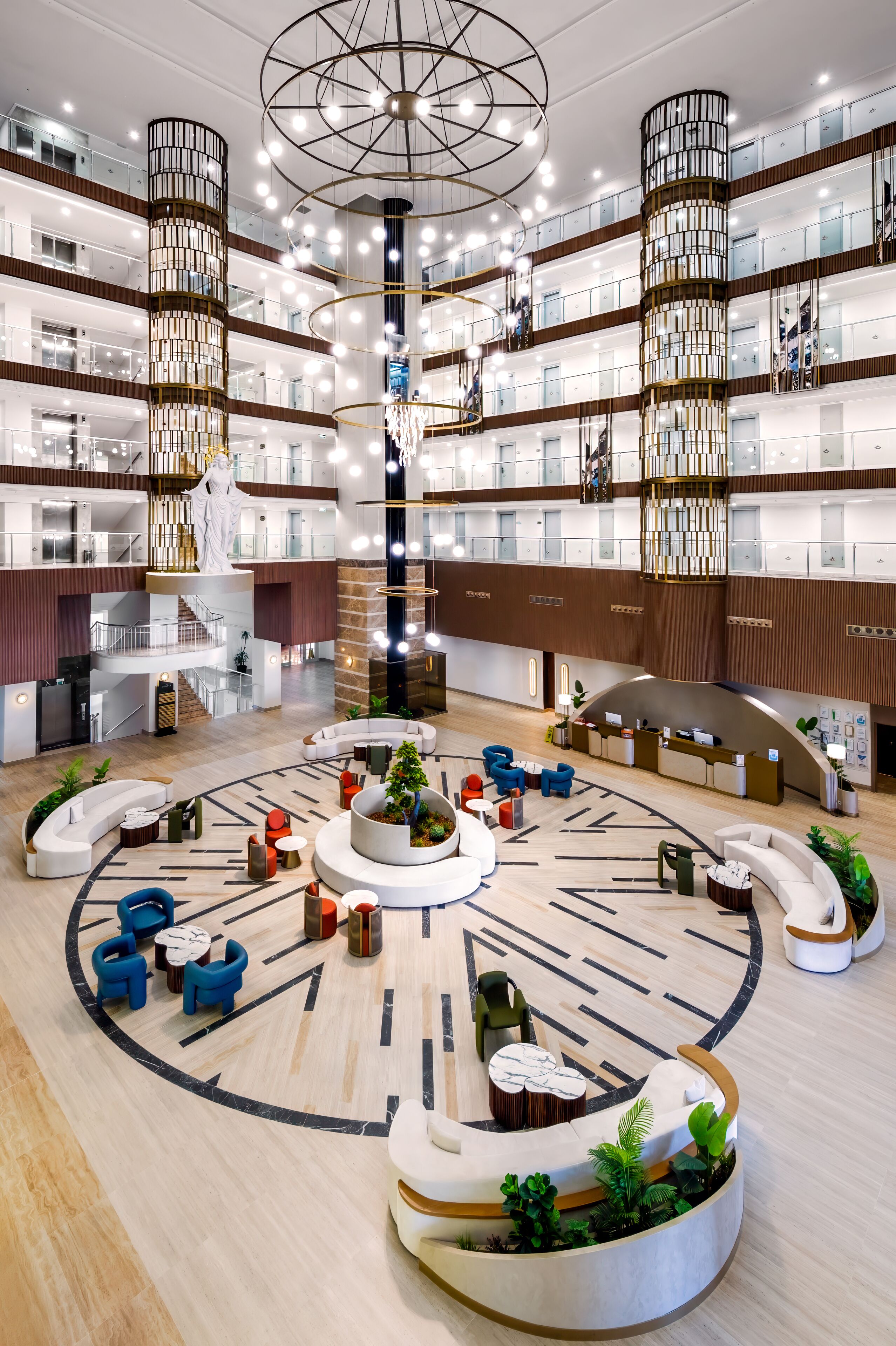 Lobby de hotel em vários níveis, com área de estar central, diversos andares e um lustre moderno.