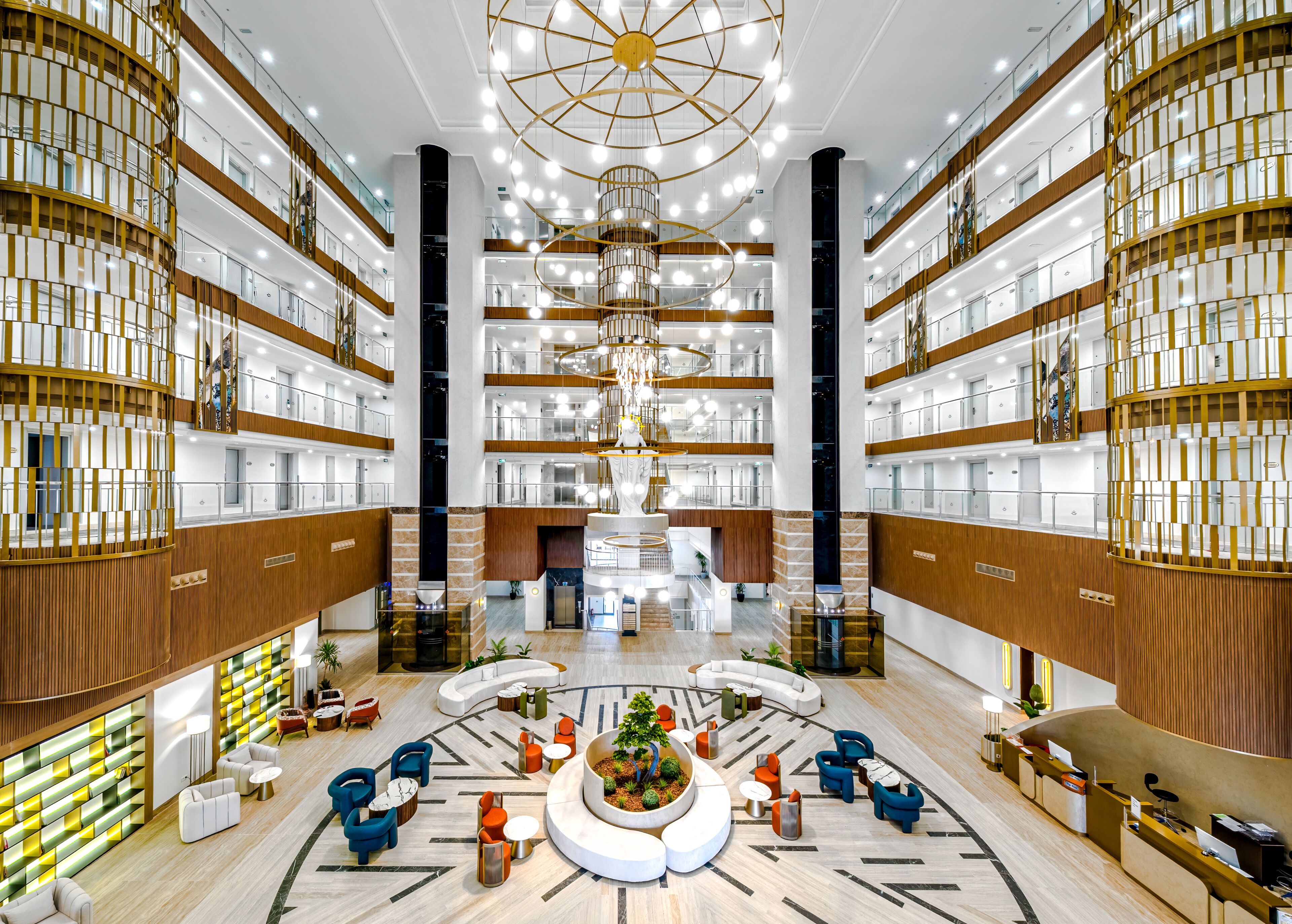 Um saguão de hotel com vários níveis, uma área de estar central, vários andares com sacadas e um lustre moderno.
