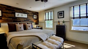 Quarto com cama, mesa de cabeceira, prateleira na parede, janela com persianas e ventilador de teto.