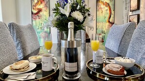 Uma mesa de jantar com uma garrafa de vinho, um arranjo floral e itens de café da manhã, como um sanduíche, café e suco de laranja.