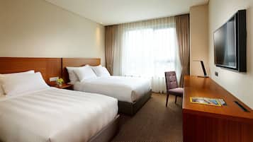 Quarto de hotel com duas camas, uma mesa, uma cadeira, televisão e janela com cortinas.