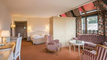 Quarto de hotel com uma cama, área de estar com sofá e poltronas, uma mesinha e uma escrivaninha com cadeira.