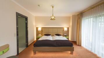 Quarto de hotel com uma cama grande, mesa de cabeceira com luminária, espelho e janela com cortinas.