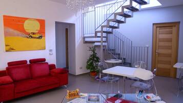 Uma sala de estar moderna com um sofá vermelho, uma mesa de centro de vidro, uma mesa branca e uma escada que leva a um andar superior.