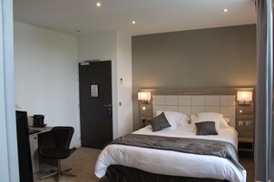 Quarto de hotel com uma cama, abajures, uma escrivaninha com computador e uma cadeira.