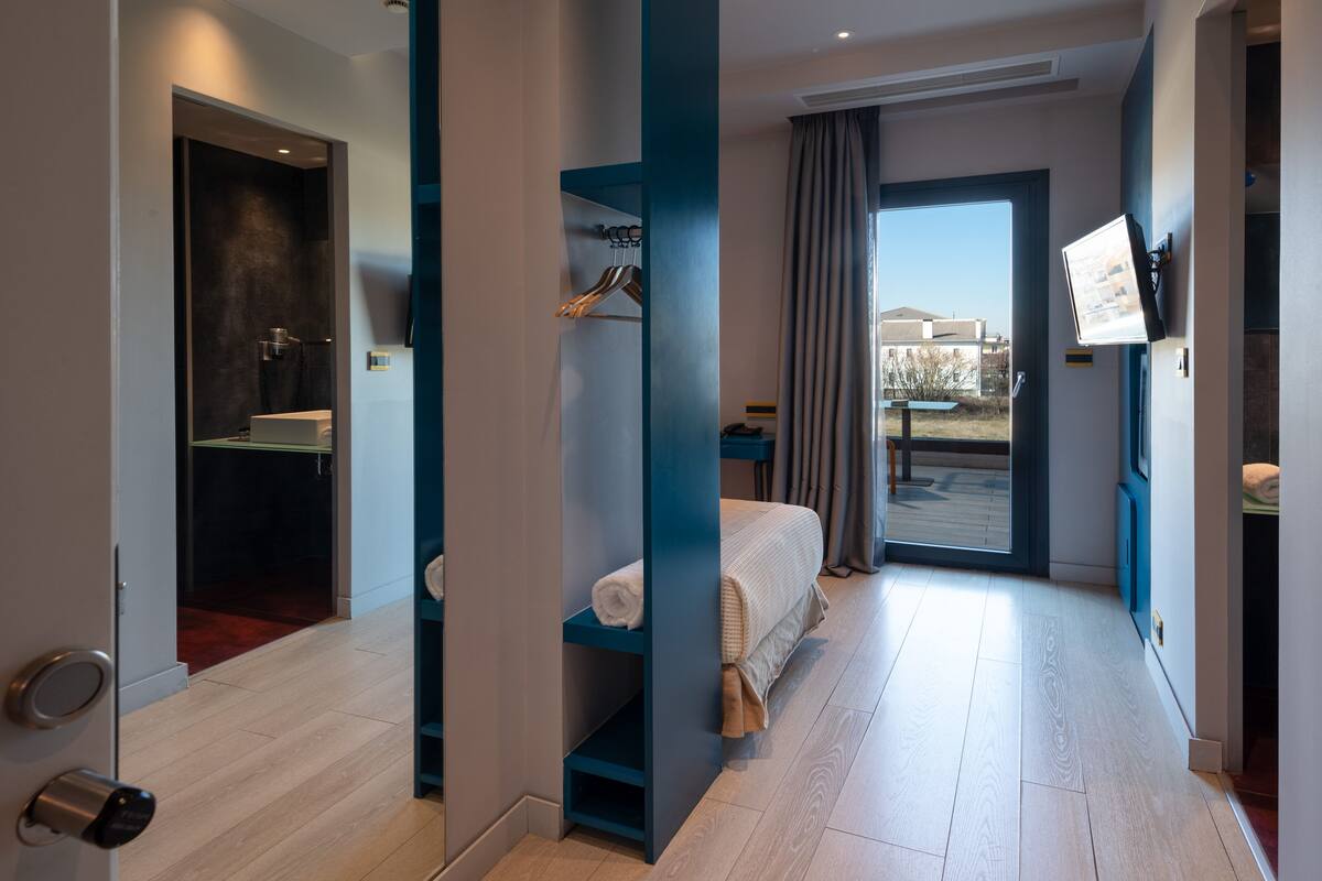Quarto de hotel moderno com cama, armário embutido, área de chuveiro e vista para o exterior.