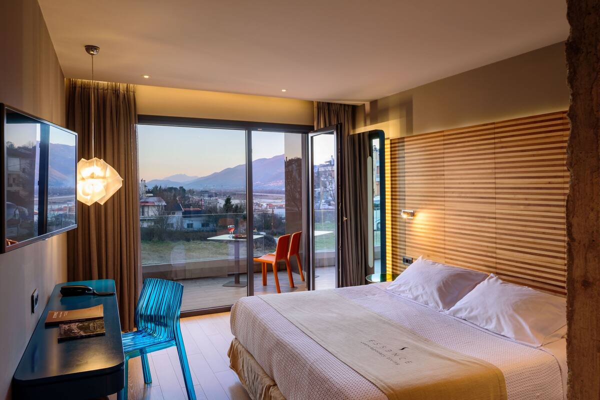Quarto de hotel com uma cama grande, uma escrivaninha, uma cadeira e uma varanda com vista para a cidade.