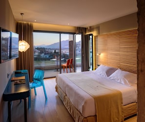 Quarto de hotel com cama grande, escrivaninha, cadeira e varanda com vista.