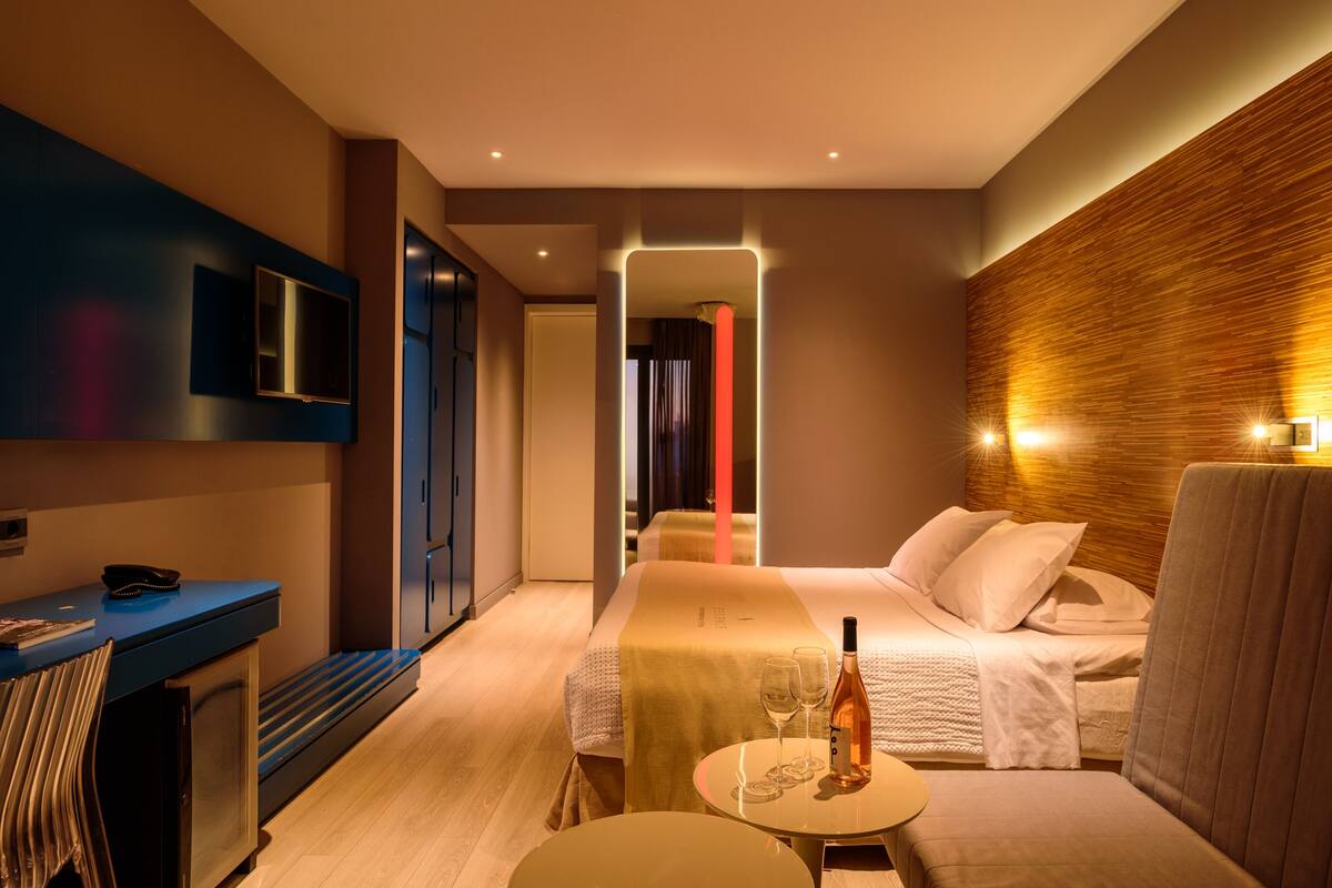 Quarto de hotel moderno com cama, mesa de cabeceira e televisão presa à parede.