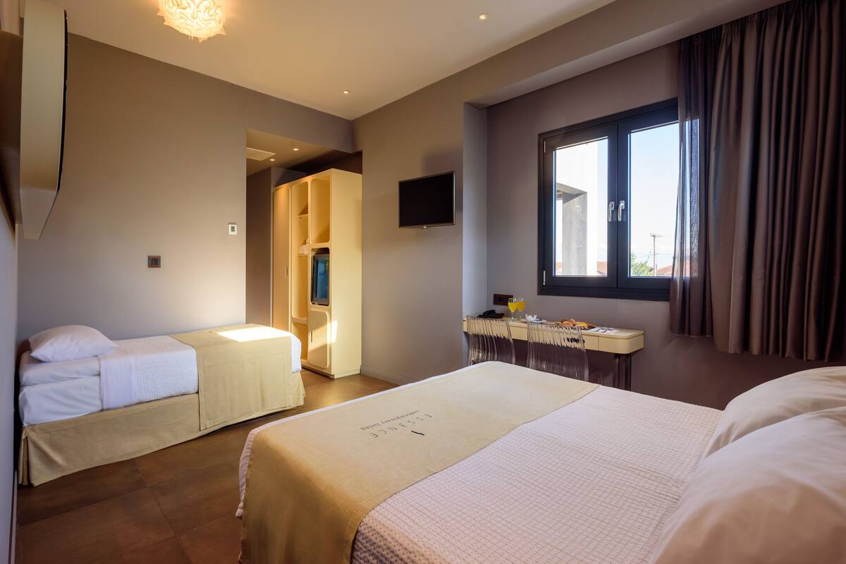 Quarto de hotel com duas camas, uma escrivaninha, uma televisão e uma janela com cortinas.