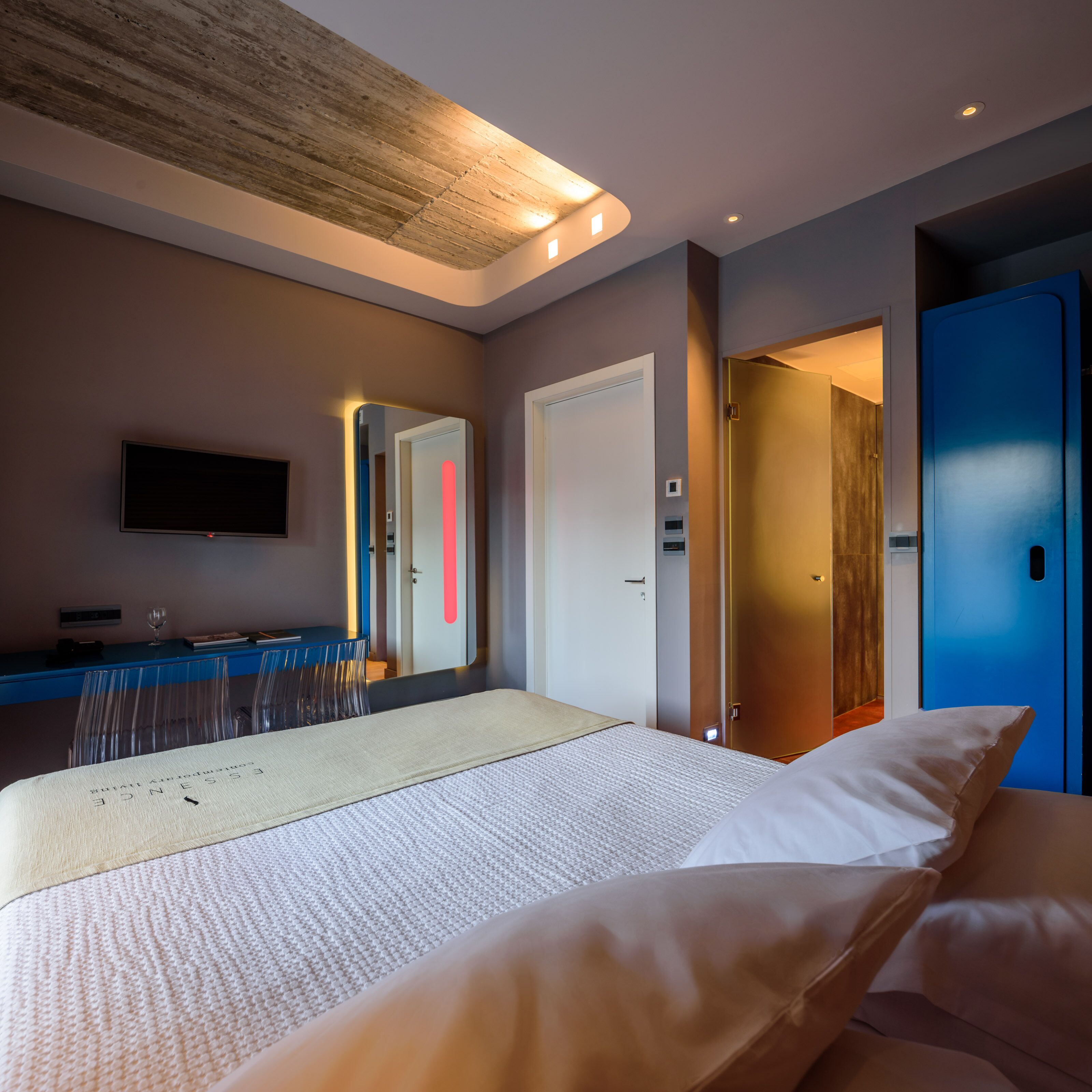 Quarto de hotel moderno com uma cama grande, uma escrivaninha, televisão de tela plana e banheiro visível por uma porta aberta.