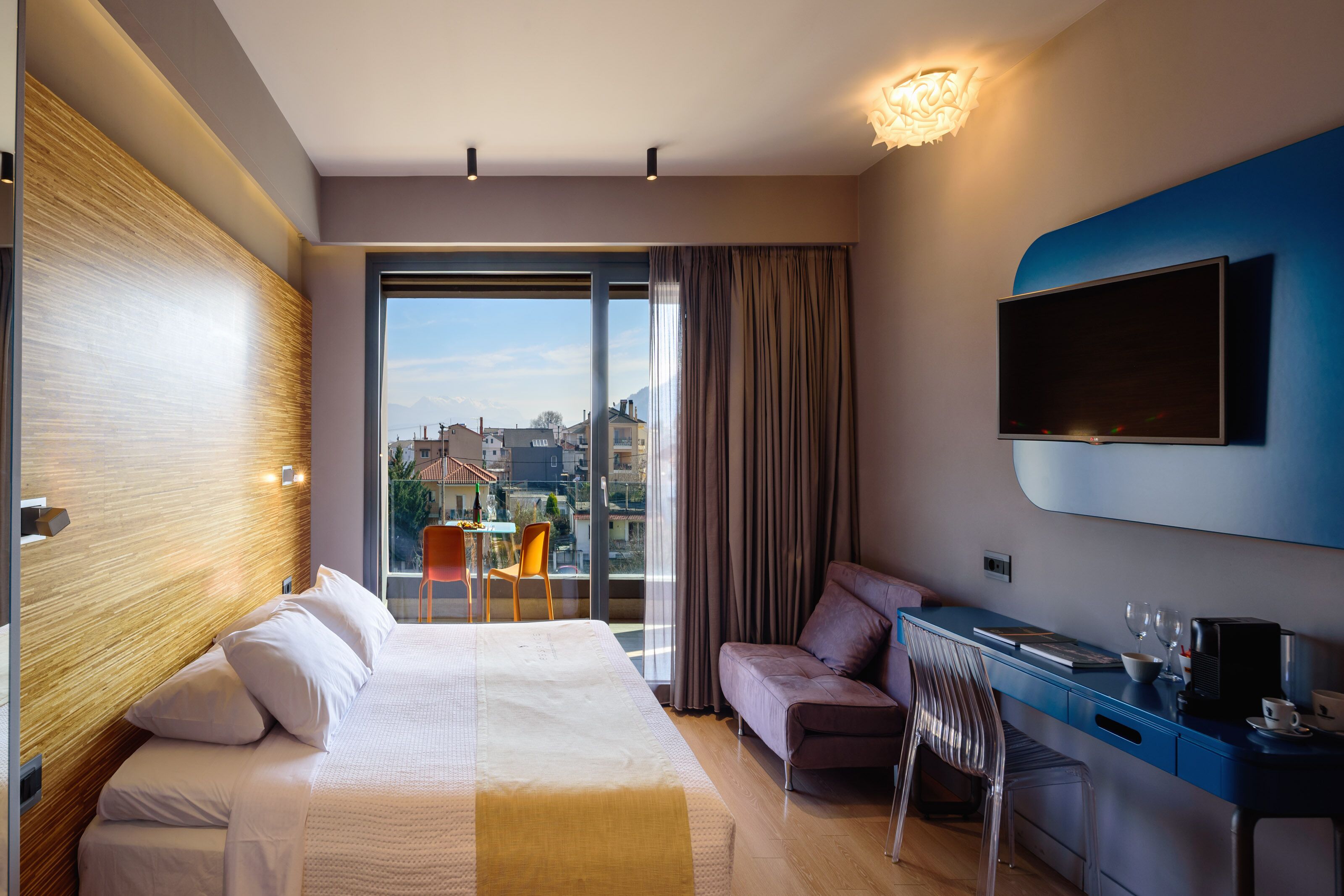 Quarto de hotel com uma cama grande, uma mesa com cadeira, uma TV fixada na parede e vista para a cidade pela janela.