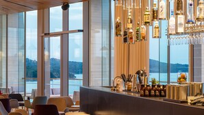 Uma área de bar moderna com um balcão comprido, banquetas e vista para o exterior.