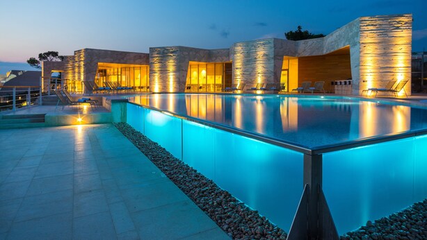 Um hotel moderno com piscina, área externa para descanso e fachada bem iluminada.