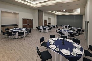 Sala de conferências com várias mesas dispostas para reuniões, equipada com cadeiras e mesas, e uma tela grande para apresentações.