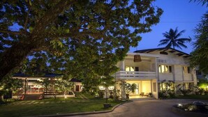 Uma casa de dois andares com varanda, entrada por meio de calçada e gramado bem cuidado.
