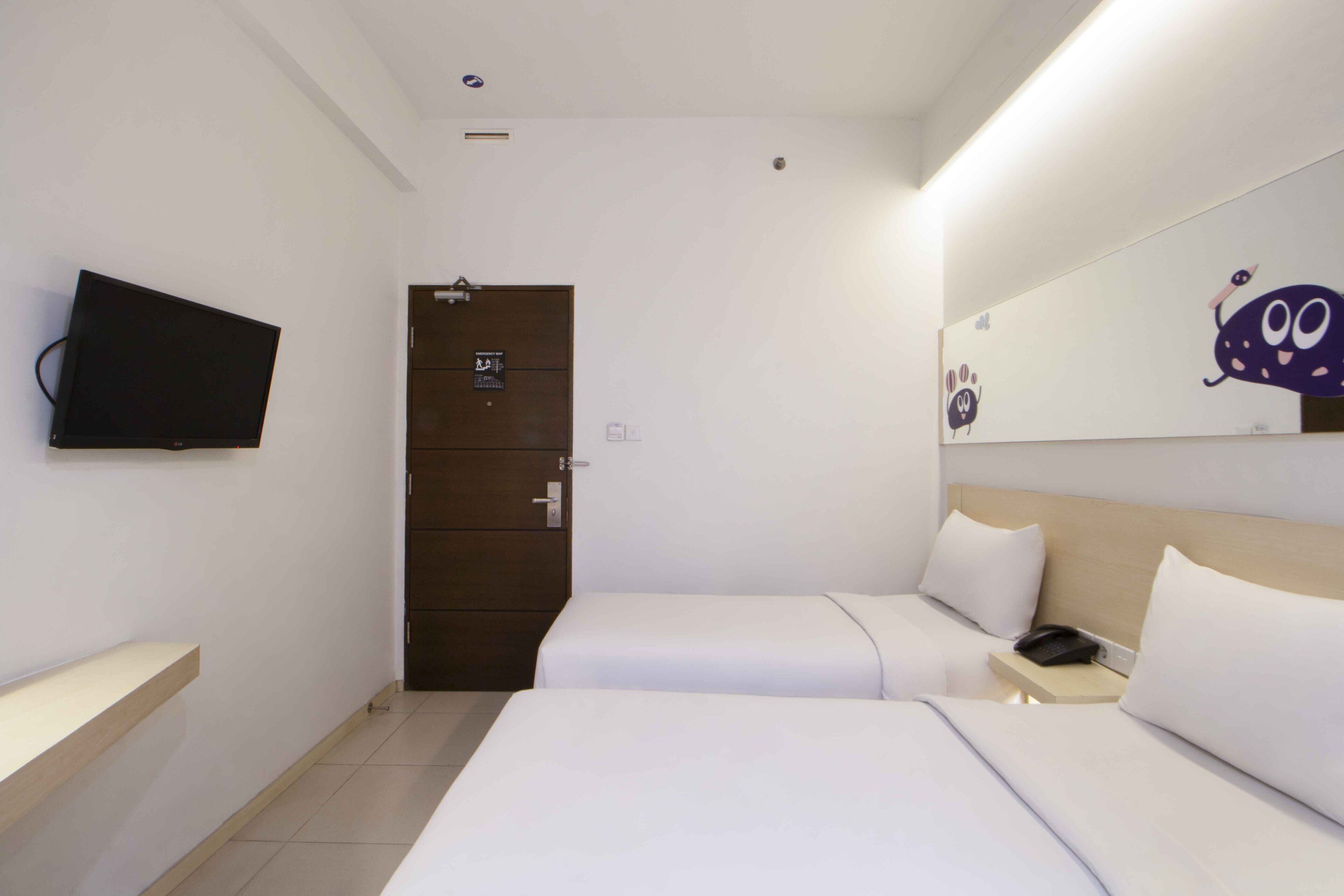 Quarto de hotel com duas camas, uma televisão, uma porta e um espelho com um personagem de desenho animado.