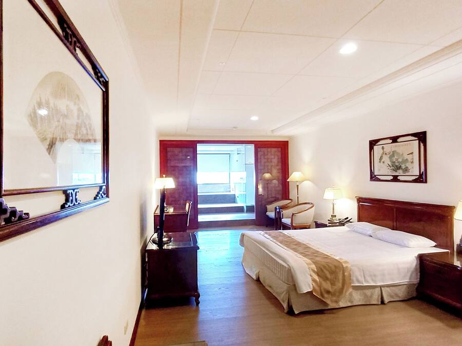 Quarto de hotel com cama grande, luminárias de cabeceira, escrivaninha e espelho.