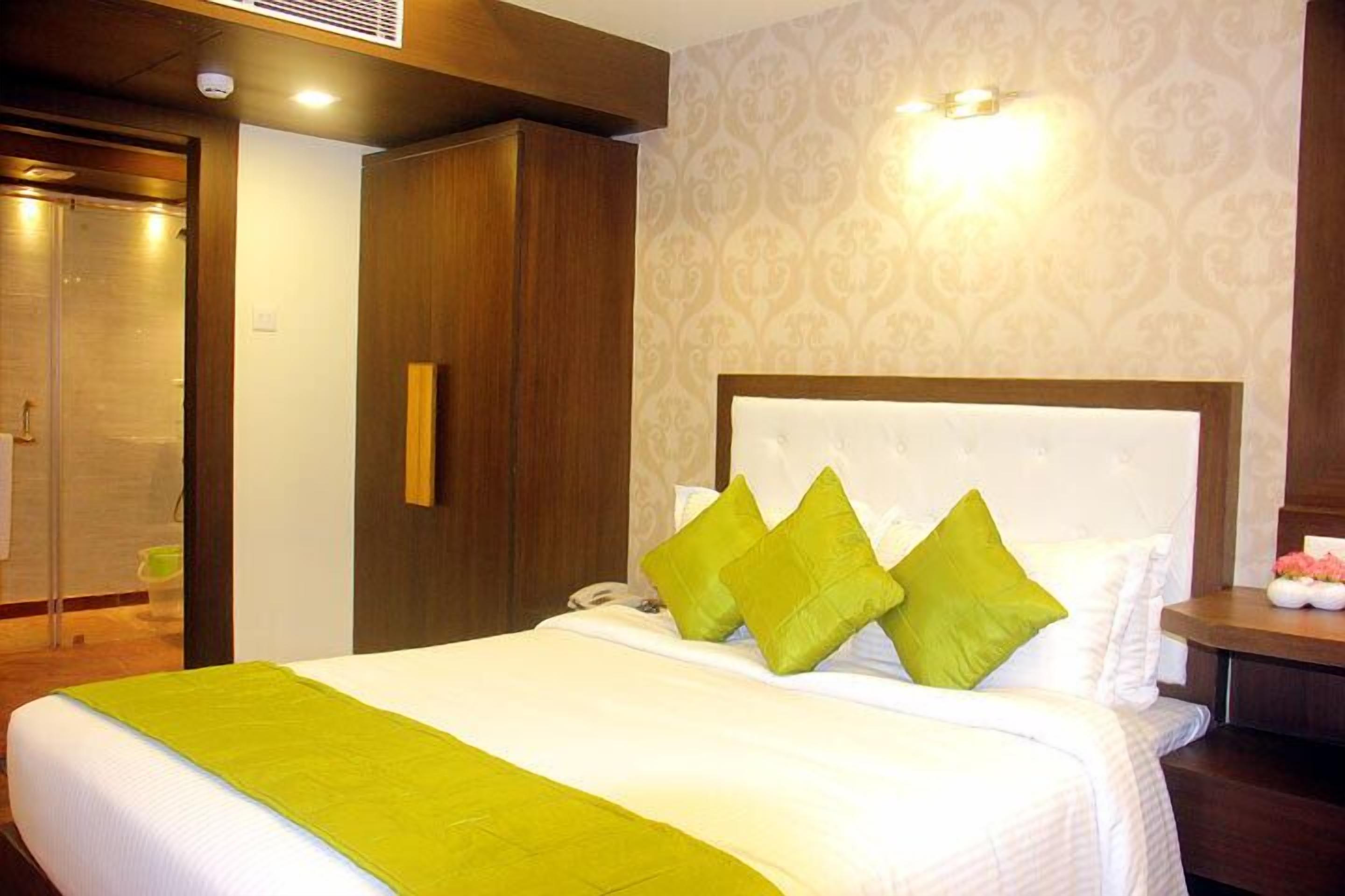 Quarto de hotel com uma cama grande, um guarda-roupa de madeira, uma mesa de cabeceira com um vaso de flores e um papel de parede estampado.