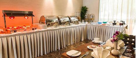 Uma mesa de buffet com várias estações de serviço, uma longa mesa de jantar com toalhas e uma grande janela com cortinas.
