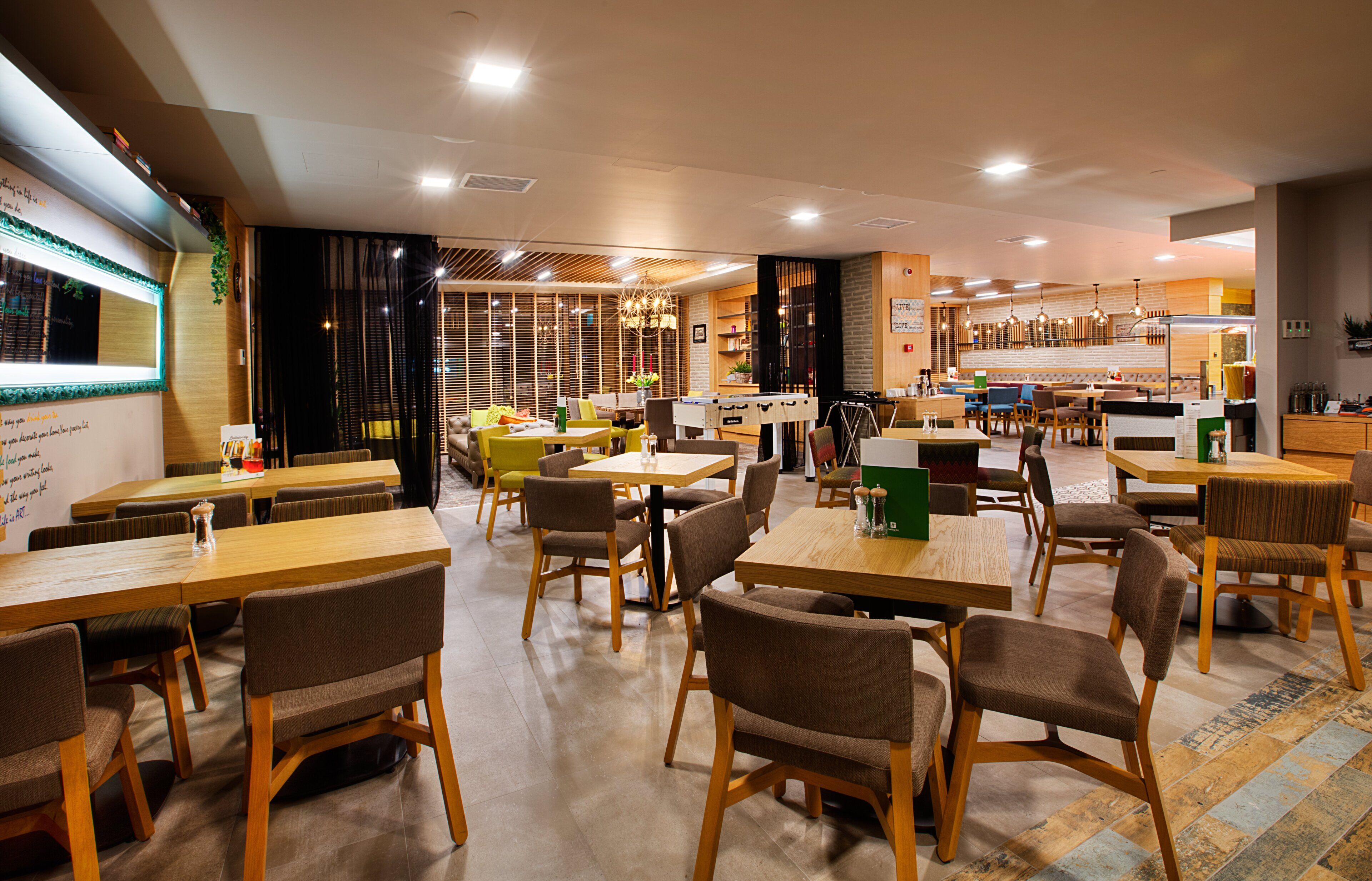 Interior moderno de restaurante com mesas e cadeiras de madeira, um espaço de bar e vista para a cozinha.