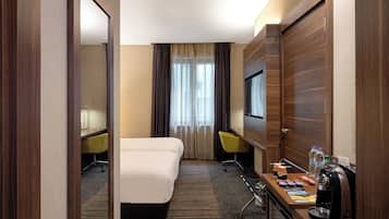 Quarto de hotel com uma cama, uma mesa com cafeteira, uma cadeira e uma televisão.