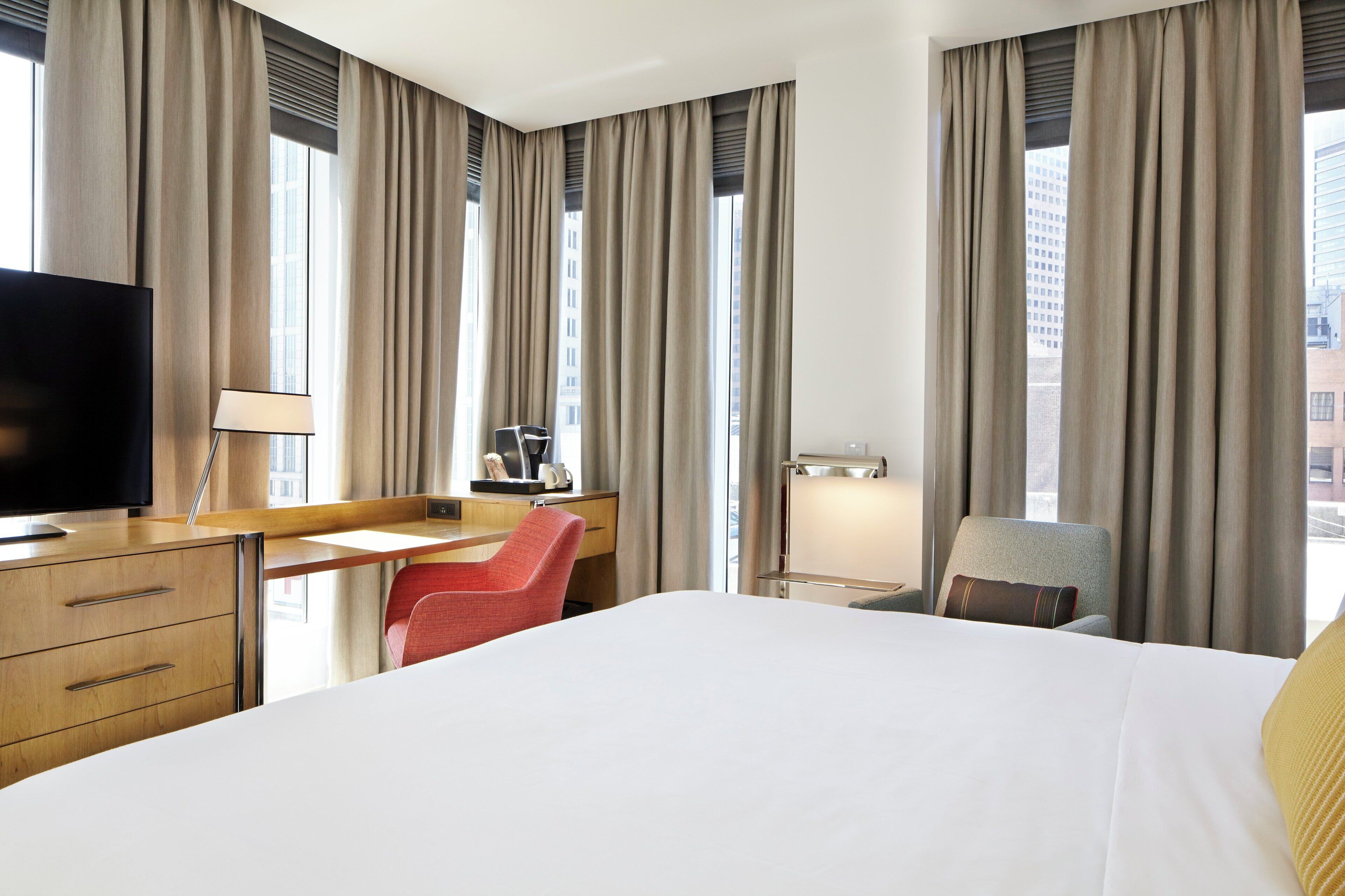 Quarto de hotel com cama, escrivaninha, televisão e uma cadeira.