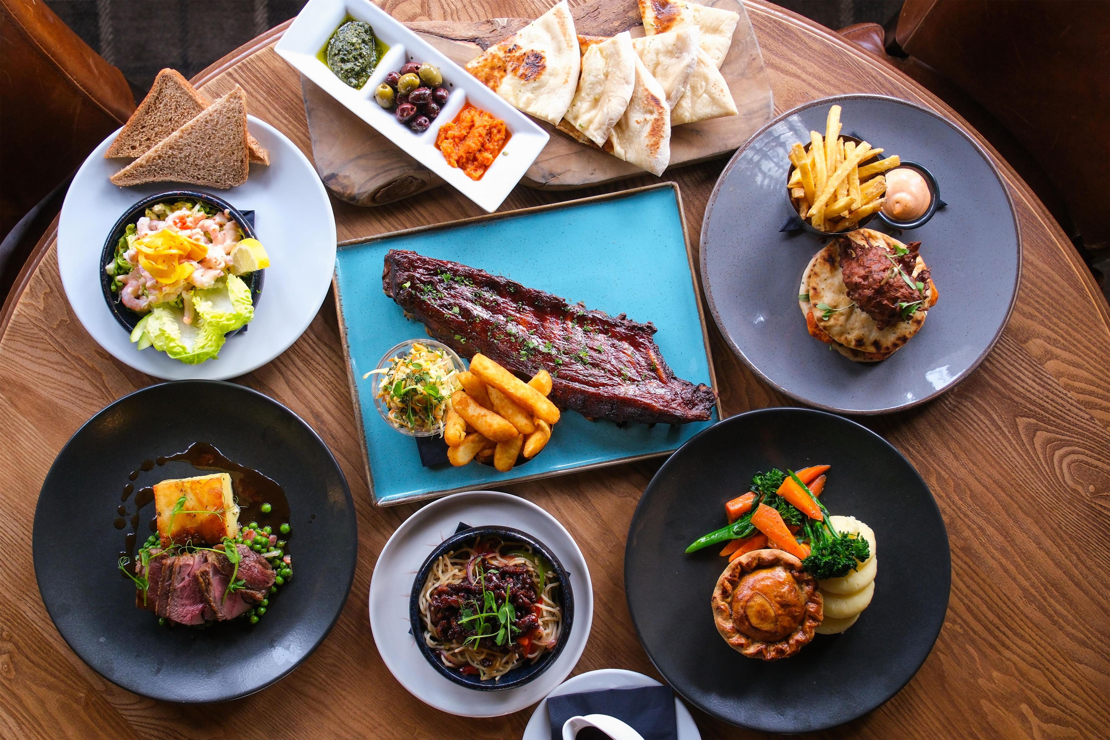 Mesa redonda com diversos pratos, incluindo bife, batatas fritas e uma salada.