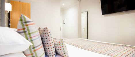 Quarto de hotel com cama, almofadas, televisão e guarda-roupa.