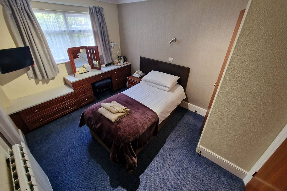 Quarto de hotel com cama, escrivaninha, espelho, televisão e janela com cortinas.