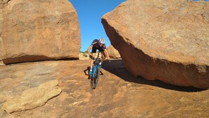 Um ciclista pedala por um terreno rochoso com grandes pedras.