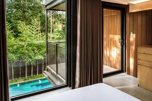 Quarto com uma grande janela com vista para uma piscina e vegetação exuberante.