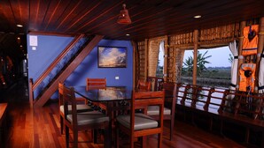 Uma sala de jantar de madeira com mesa e cadeiras de vidro, uma escada e vista para o exterior.