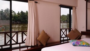 Quarto com uma grande janela com vista para um corpo d'água, uma cama com almofadas e um corrimão de madeira.