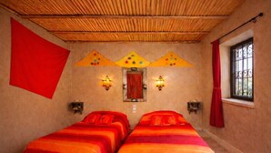 Quarto com duas camas, um adorno na parede vermelho, luminárias fixadas na parede e uma janela com cortina.