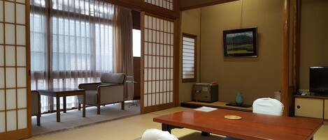 Um quarto japonês tradicional com tatames, uma mesa baixa, um sofá e portas deslizantes.