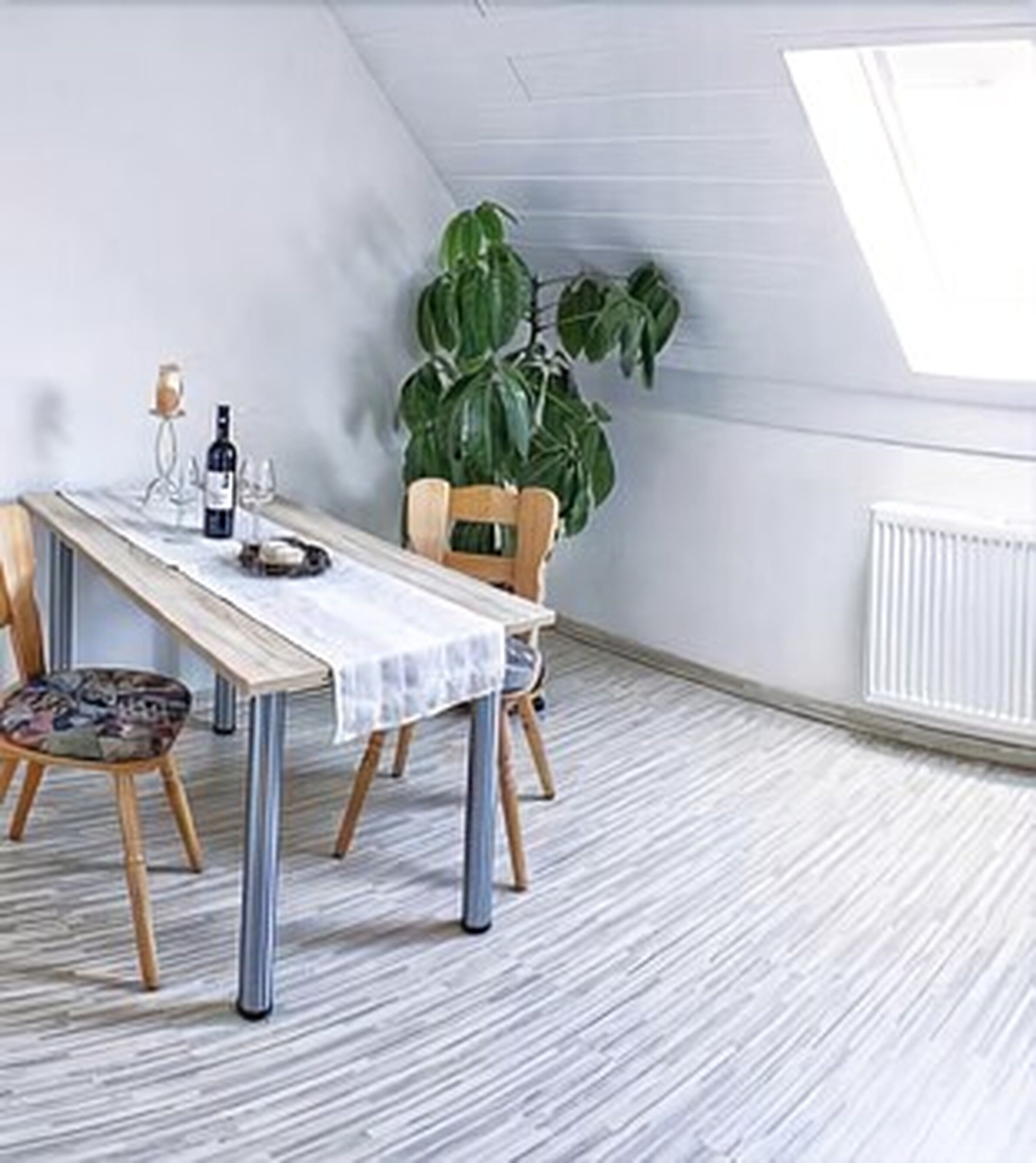 Uma sala de jantar com mesa de madeira, cadeiras, uma planta em vaso e um radiador.
