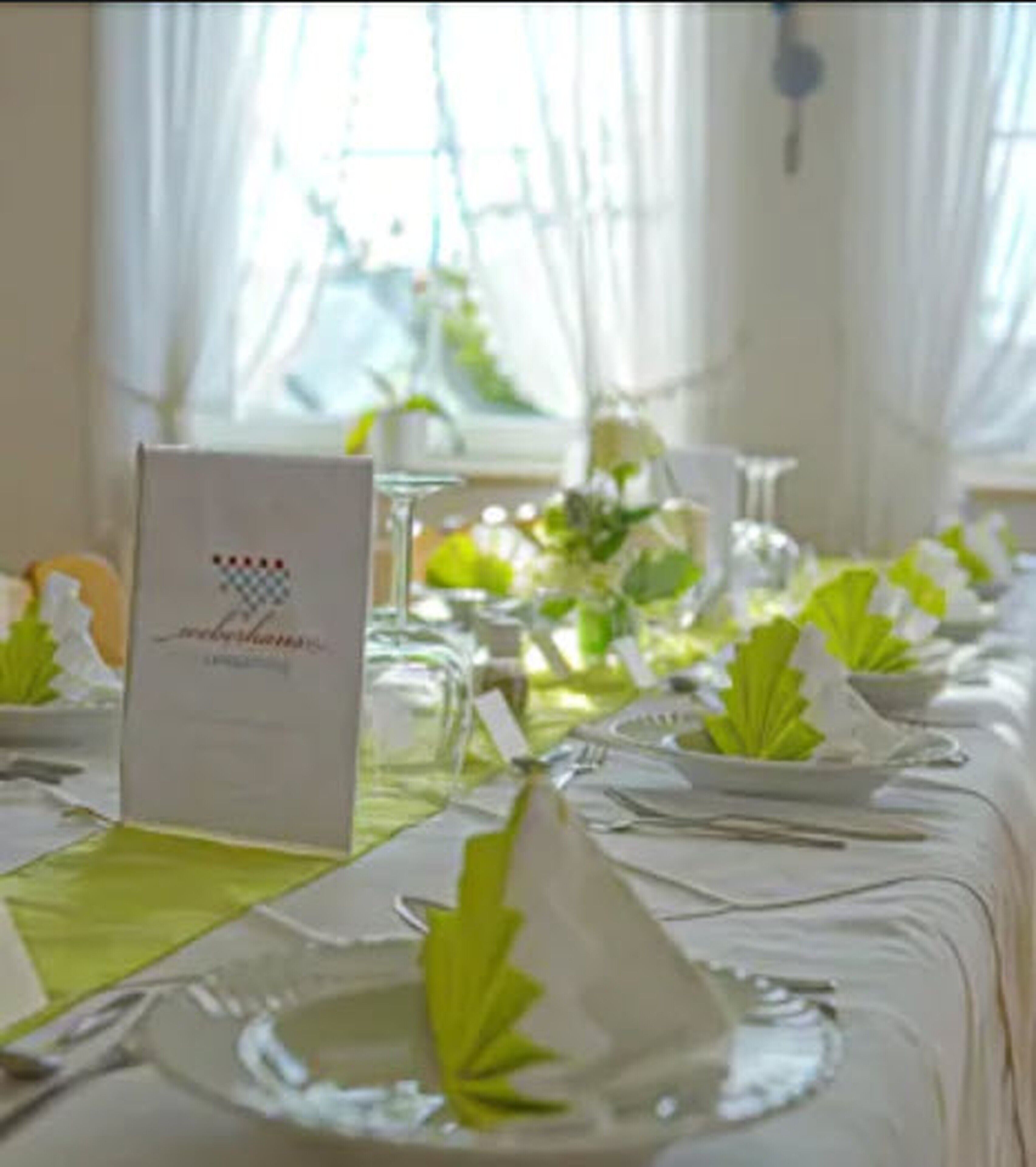 Uma mesa posta com toalhas brancas, guardanapos verdes e copos de vidro transparente.