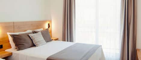 Quarto de hotel com duas camas, cabeceira, ar condicionado, janela com cortinas e luminária no teto.