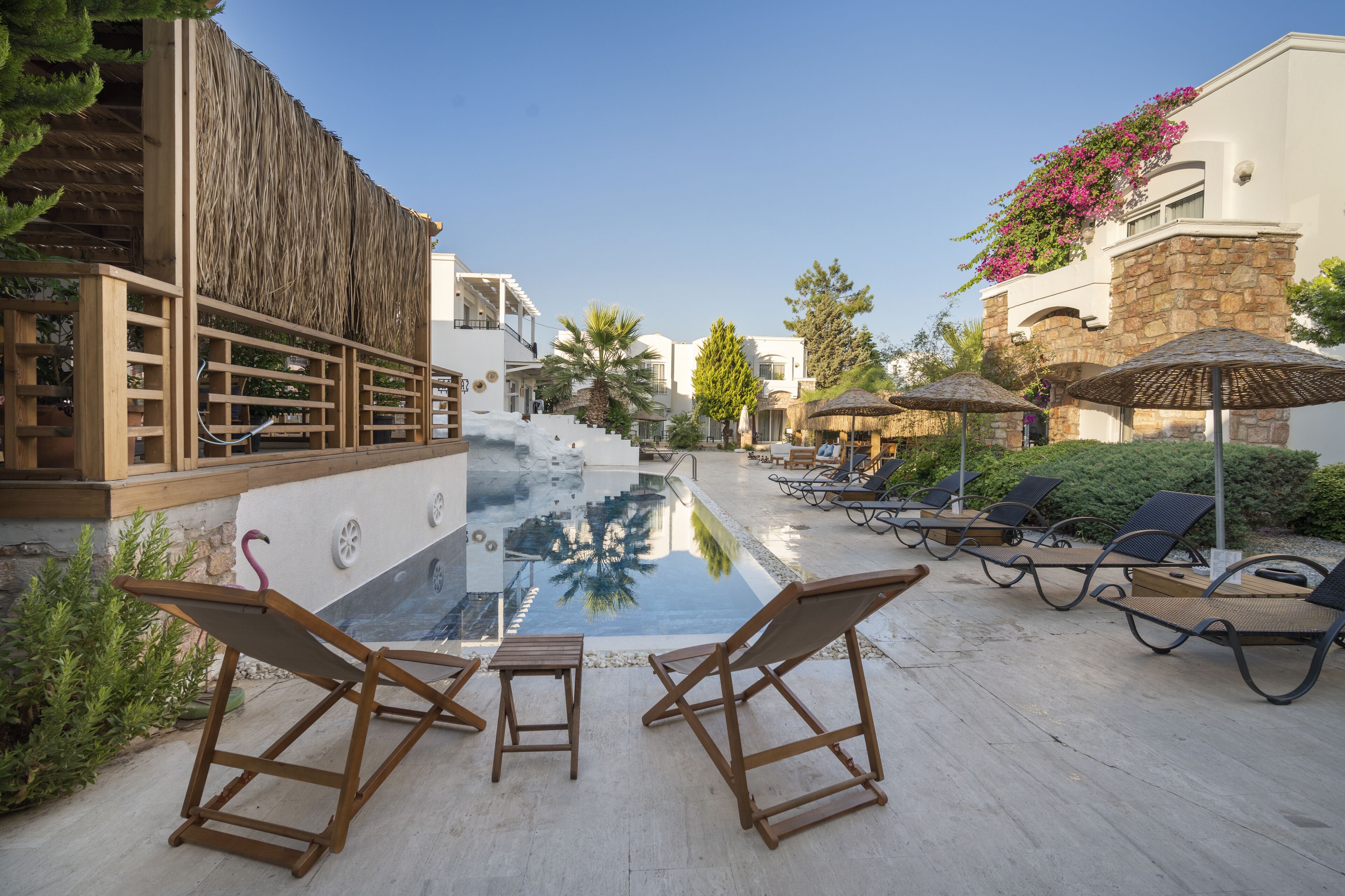 Uma área à beira da piscina com espreguiçadeiras, um deck de madeira e um edifício de pedra com piscina.