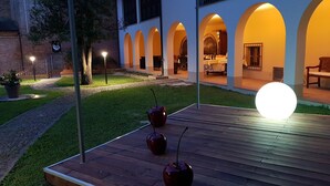 Um pátio com deck de madeira, três vasos grandes e uma luminária iluminada.