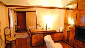 Quarto de hotel com piso de madeira, área de jantar com mesa e cadeiras, televisão e lareira.