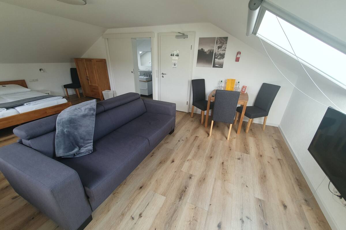 Um espaço compacto para viver, com sofá, mesa de jantar e cadeiras, cama e pequeno espaço de cozinha.