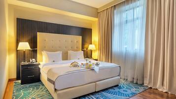 Quarto de hotel com uma cama grande, duas luminárias de cabeceira, mesa de cabeceira e janela com cortinas.